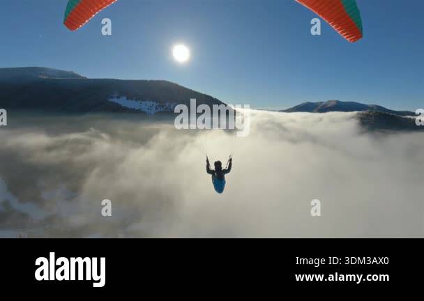 Dreamy paragliding flight high above misty clouds over winter mountains ...