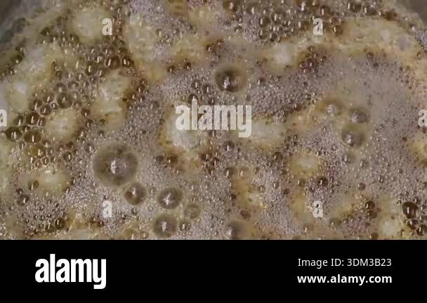 Hot cooking oil boils rapidly with large bubbles forming on the surface ...