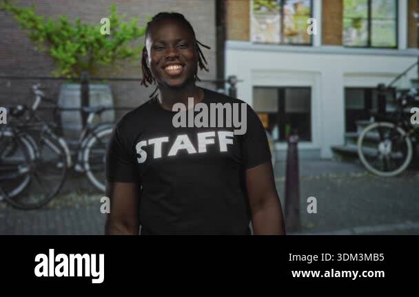Young man wearing staff tshirt smiling and finger pointing to shirt on ...