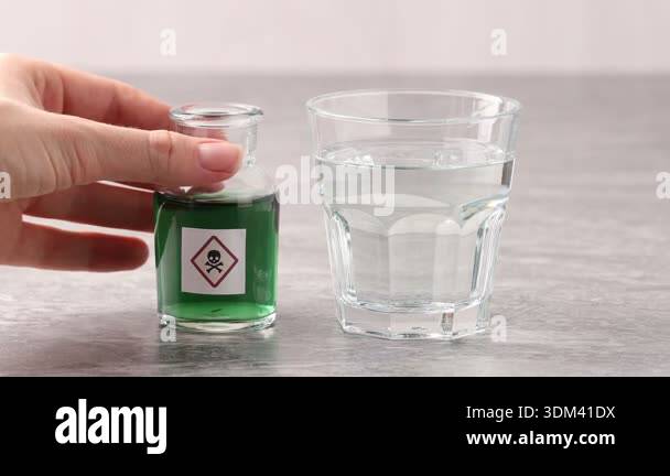 Woman pouring poison from bottle into glass with water at gray table ...