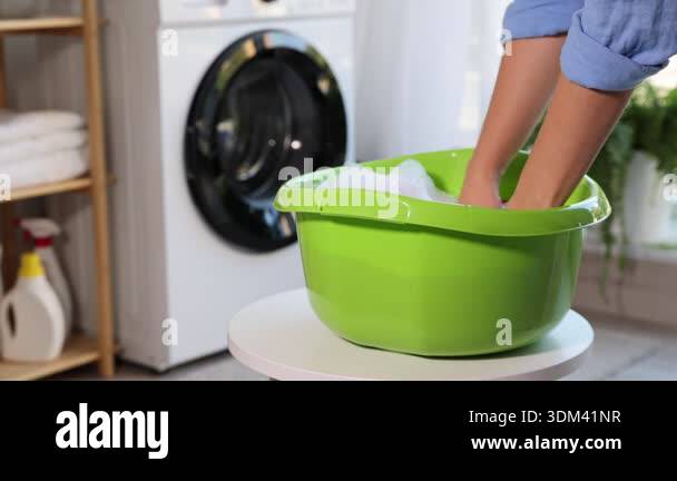 Woman washing clothes in plastic basin at white table indoors, closeup ...