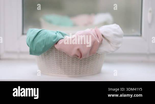 Clothes falling into plastic laundry on windowsill indoors, closeup ...