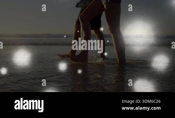couple stepping into shallow surf at sunset causing splashes and ...