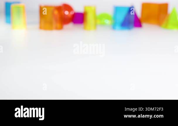 A hand manipulates a blue triangular prism among vibrant 3D shapes on a ...
