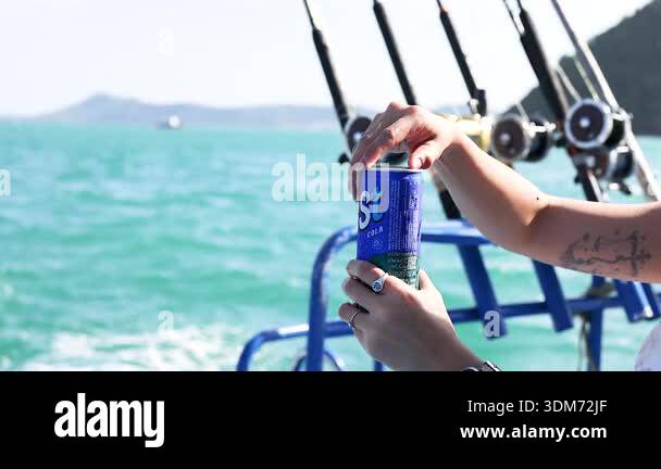 A person opens a soda can on a boat, surrounded by fishing rods and a ...