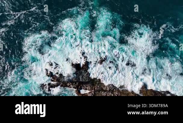 Turquoise water splashes on the rocky shore. Ocean tide hits the rocks ...