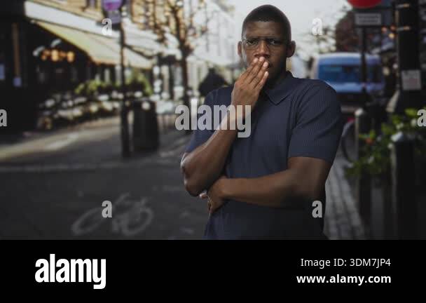 Man covering mouth with hand and wearing glasses on street, arms ...
