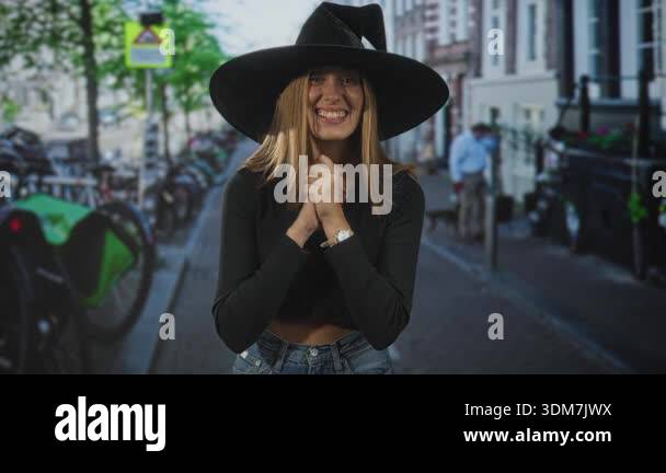 Young woman in witch hat clasping hands and smiling broadly, showing ...