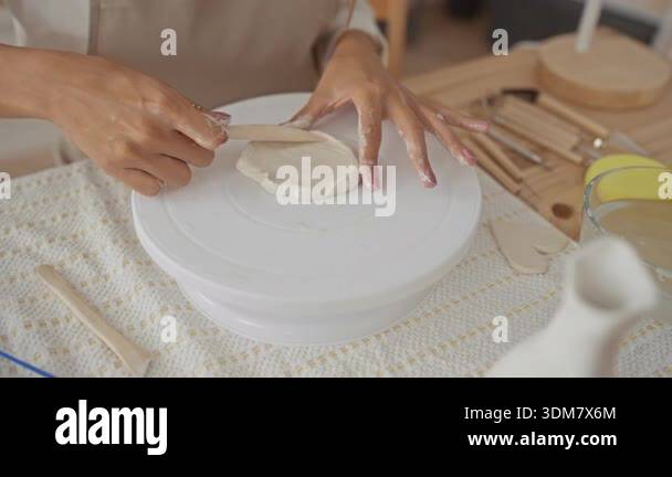 Woman smooths clay disc with a wooden tool in pottery studio ...