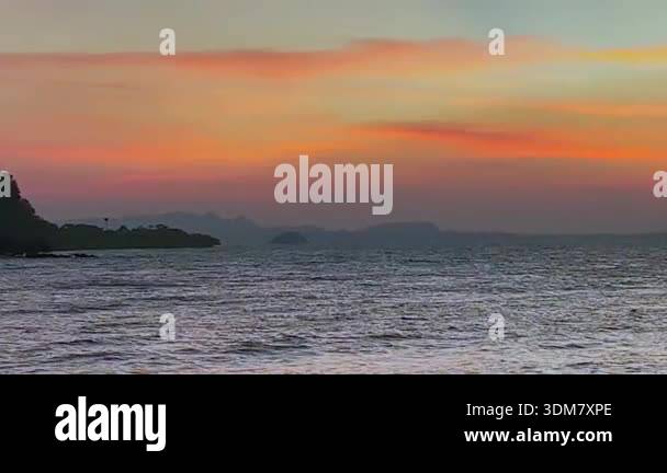Sunset over calm coastal waters with soft ripples and colorful sky ...