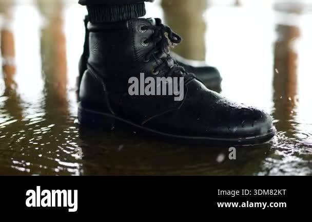 Close-up of sturdy, laced black boots near water ripples. Black leather ...
