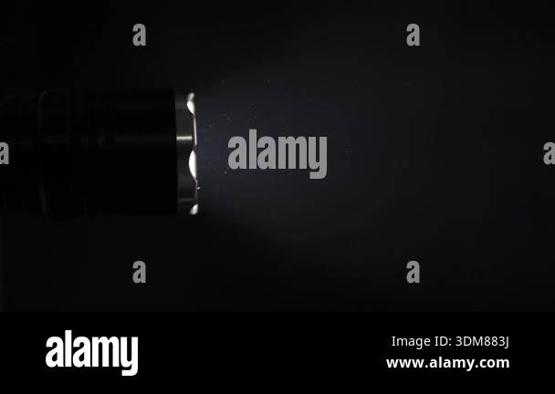 Tactical flashlight shines a bright beam, illuminating floating dust ...