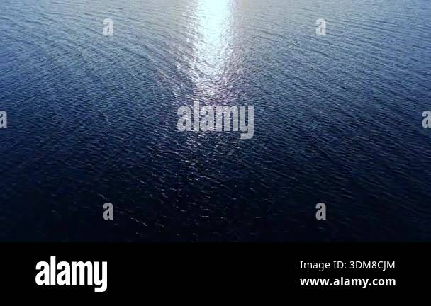 Close-up aerial shot of dark blue water surface with sun glisten and ...