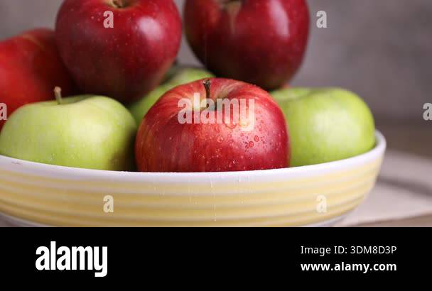 Spraying red and green apples with water in bowl on table against grey ...