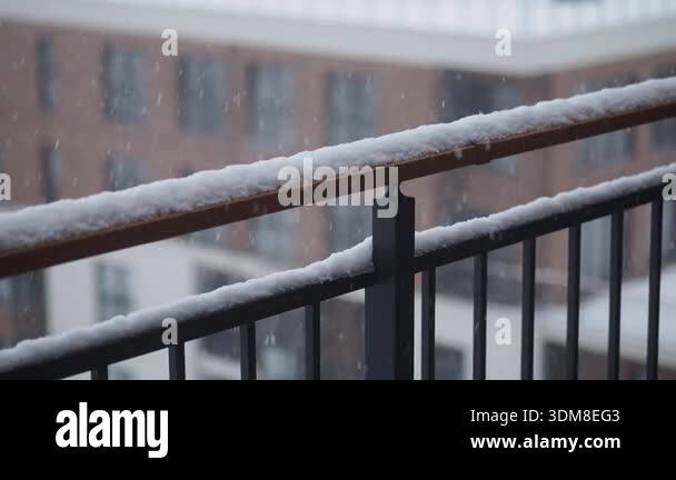 Snow falls on a balcony railing in a city setting during winter Stock ...