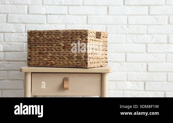 Clothes falling into laundry basket on table near white brick wall ...