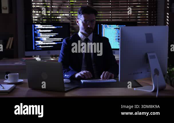 Programmer in suit and glasses working on computer and laptop at wooden ...