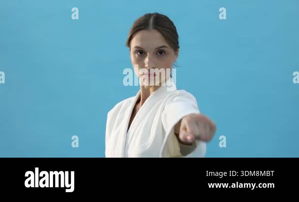 Woman in uniform practicing karate on light blue background, camera ...