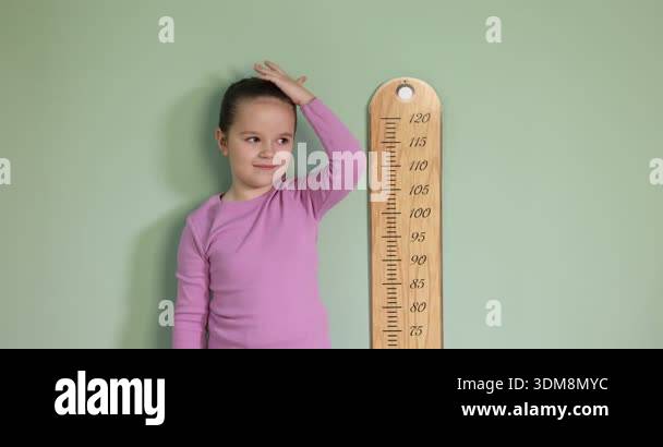 Little girl measuring her height with chart near light green wall Stock ...