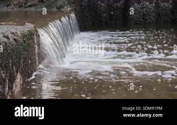 Close-up of water flowing over a concrete ledge creating a small ...