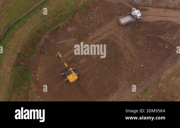 Top-down aerial view of a yellow excavator digging soil and loading ...