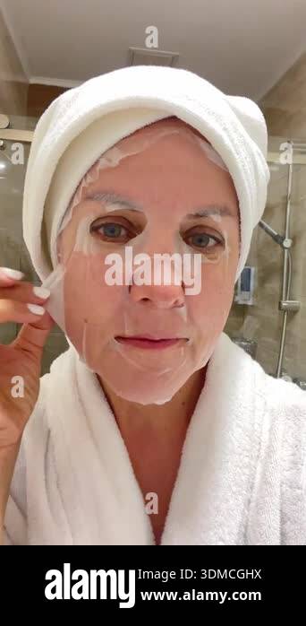 A woman in the bathroom adjusts a cloth care mask on her face. Facial ...