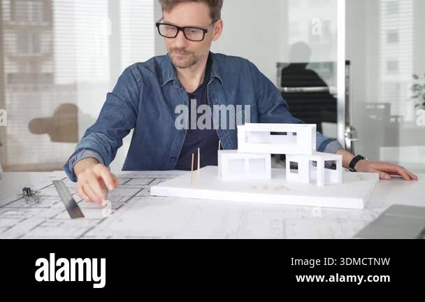 Architect drafting detailed plans at a cluttered desk with blueprints ...