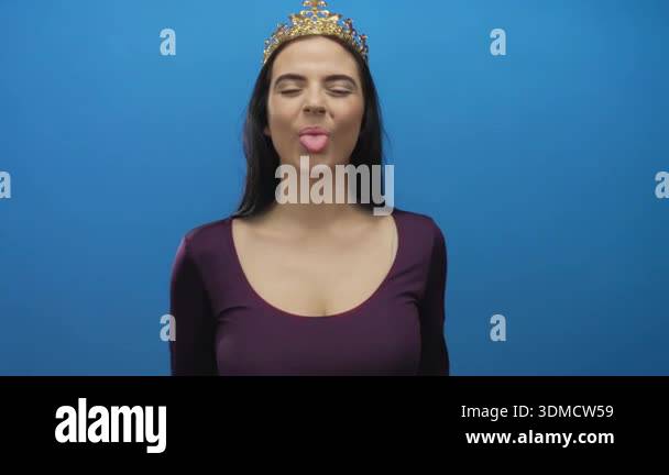 Woman wearing crown smiles against blue background showing playful ...