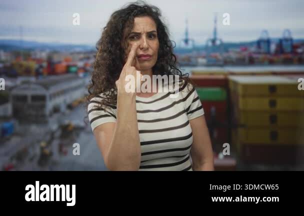 Woman pointing finger to cheek at port against stacked shipping ...