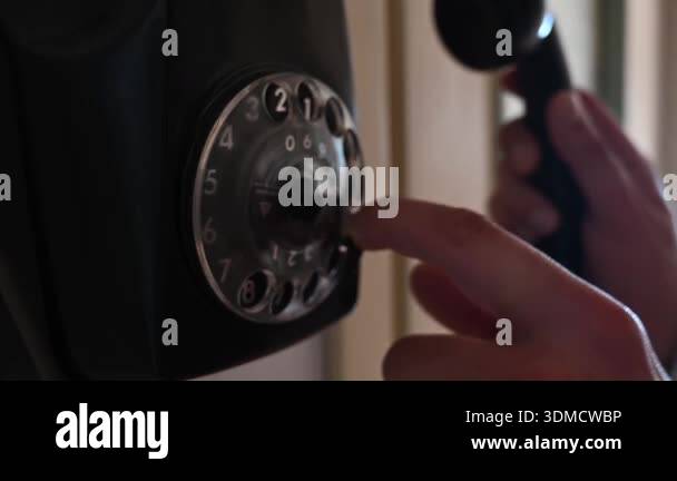 using a classic black rotary dial telephone, dialing a phone number ...