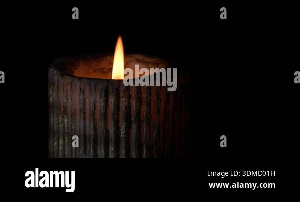 A candle sits in a dark room with a warm flame shining brightly. The ...