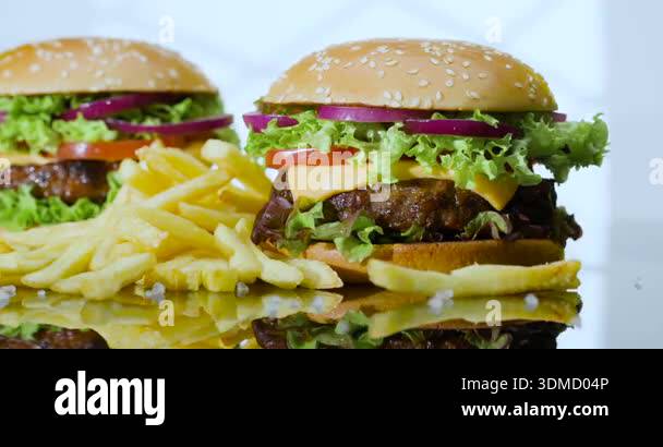 Two big burgers sit on a table next to a pile of crispy fries. The ...
