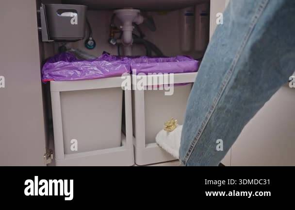 Woman disposing food scraps into trash bin under kitchen sink with ...