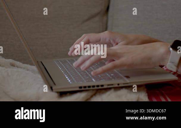 Hands typing on laptop keyboard while sitting on sofa at home. Concept ...