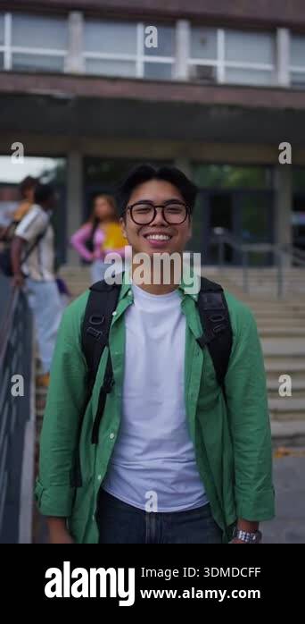 Vertical. Young Asian student with glasses and backpack smiles at the ...