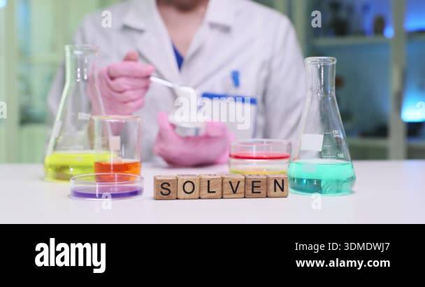 Wooden cubes spell word Solvent on laboratory table. Scientist in white ...