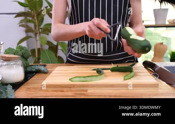 Person peels zucchini on board dropping thin green strips beside peeler ...