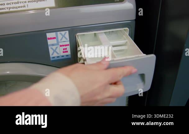 Hand places detergent into the compartment of a washing machine at a ...