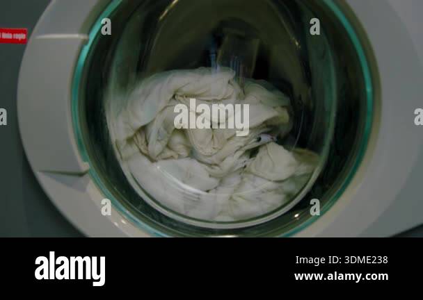 White linens spin inside a washing machine, highlighting the washing ...