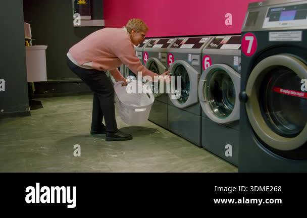 Individual in pink sweater places laundry into washing machine at self ...