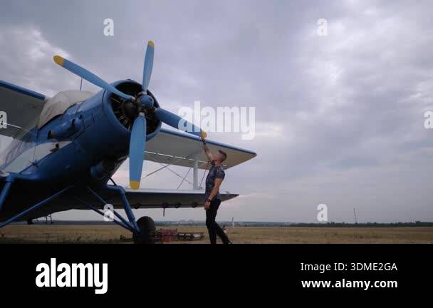 Pilot interacts with the blue biplane, examining the propeller and ...