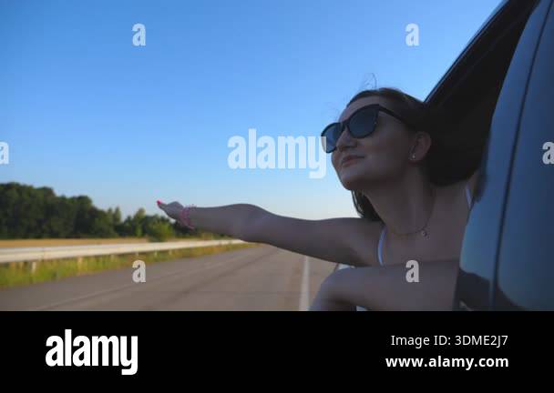 Happy girl in sunglasses leaning out of car window and enjoying trip ...