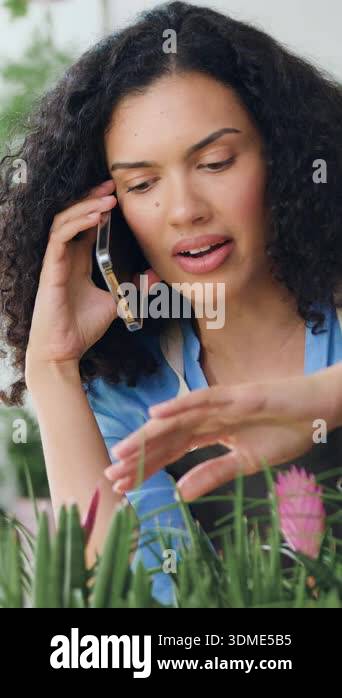 Young woman talking with customer on mobile phone and checking plants ...