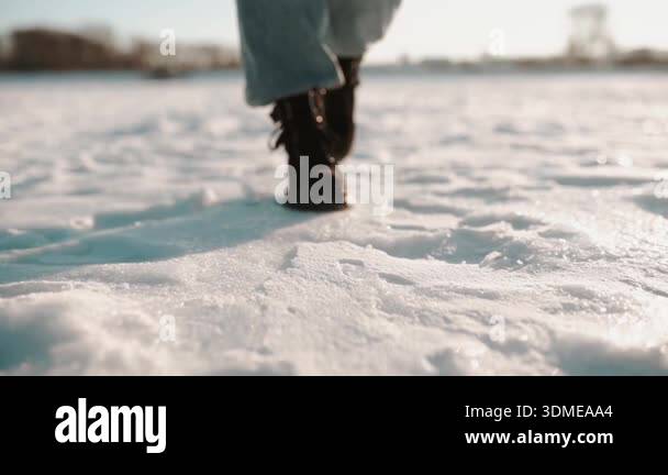 Feet in boots and jeans walking on white snow and ice in winter. The ...
