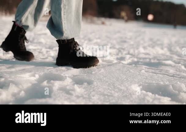 Feet in boots and jeans walking on white snow and ice in winter. The ...