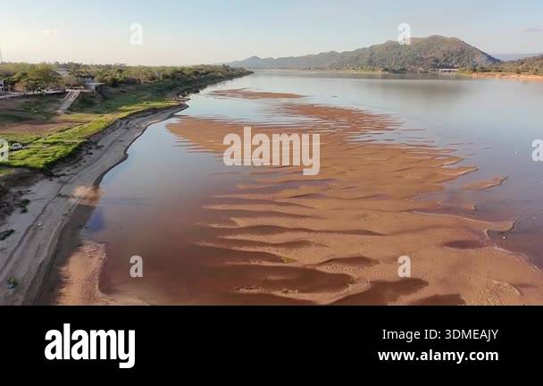 a wide river with exposed sandbanks during dry season, flowing through ...