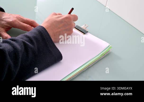 A close-up shows a hand gripping a pencil over a blank sheet clipped to ...