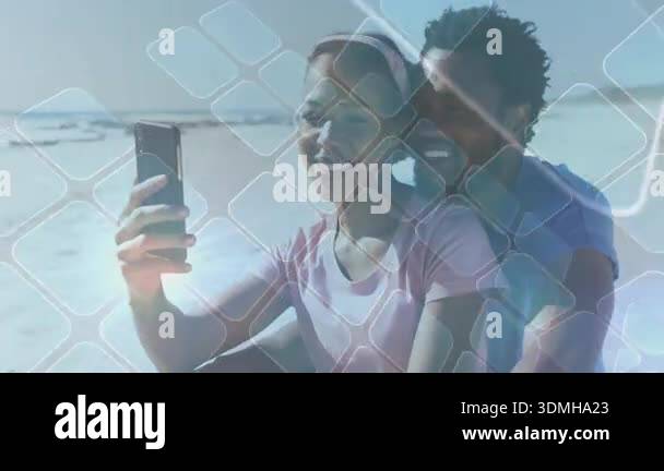 Pair sitting on beach using phone for selfie as grid overlay lens flare ...