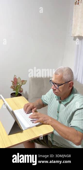 Older man wearing glasses concentrating while typing on a tablet ...