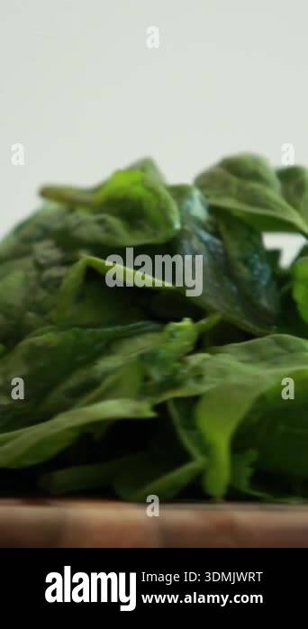 Close-up of fresh baby spinach leaves on a wooden cutting board with a ...